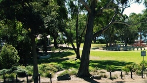 Um parque com área gramada, árvores e um pequeno edifício ao fundo.
