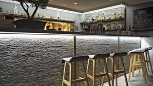 Uma área de bar com parede de pedra, banquetas de madeira e variedade de garrafas nas prateleiras.