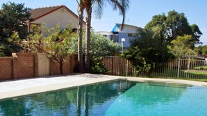 Piscina retangular com água azul cristalina, cercada por um muro de tijolos e uma grade de metal.