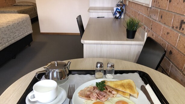 Uma bandeja de café da manhã com ovos, presunto, torradas e uma xícara de café sobre uma mesa em quarto de hotel.