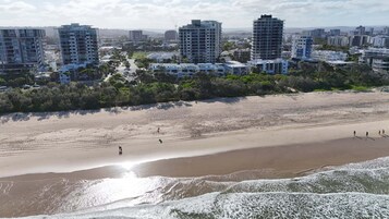 Paisagem costeira com edifícios altos, uma praia de areia e céu claro.