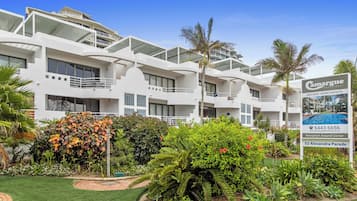Um hotel moderno de vários andares com varandas, rodeado por vegetação exuberante e palmeiras.