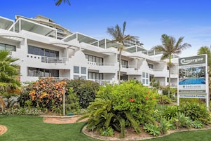 Um hotel moderno de vários andares com varandas, rodeado por vegetação exuberante e palmeiras.