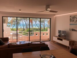 Uma sala de estar moderna com uma grande porta de vidro deslizante que dá para uma varanda com vista para o mar.