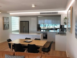 Uma cozinha moderna com uma ilha central, uma área de refeições com mesa de madeira e cadeiras pretas, e uma grande janela que oferece luz natural.