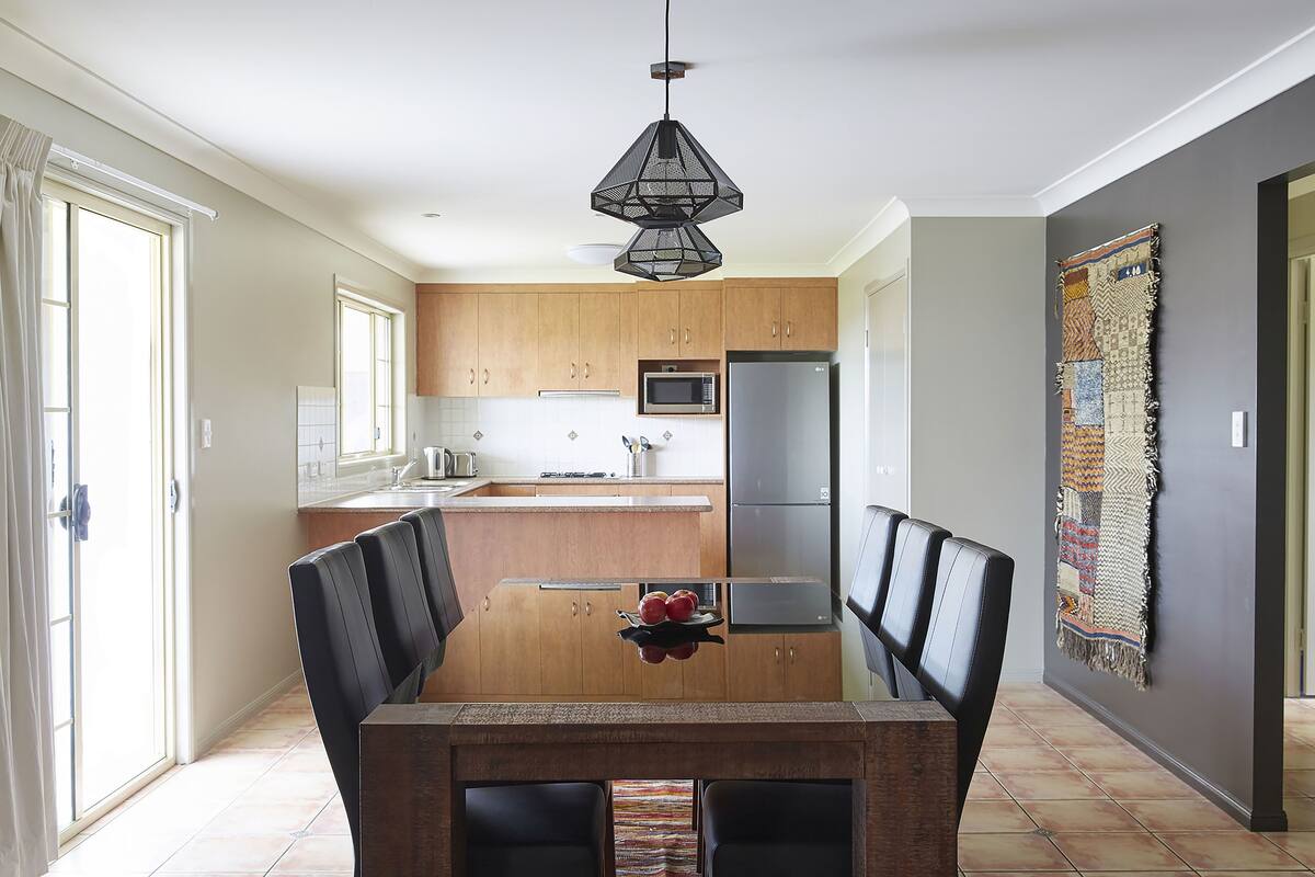 Uma cozinha moderna com armários de madeira, uma mesa de jantar de vidro e um lustre preto.