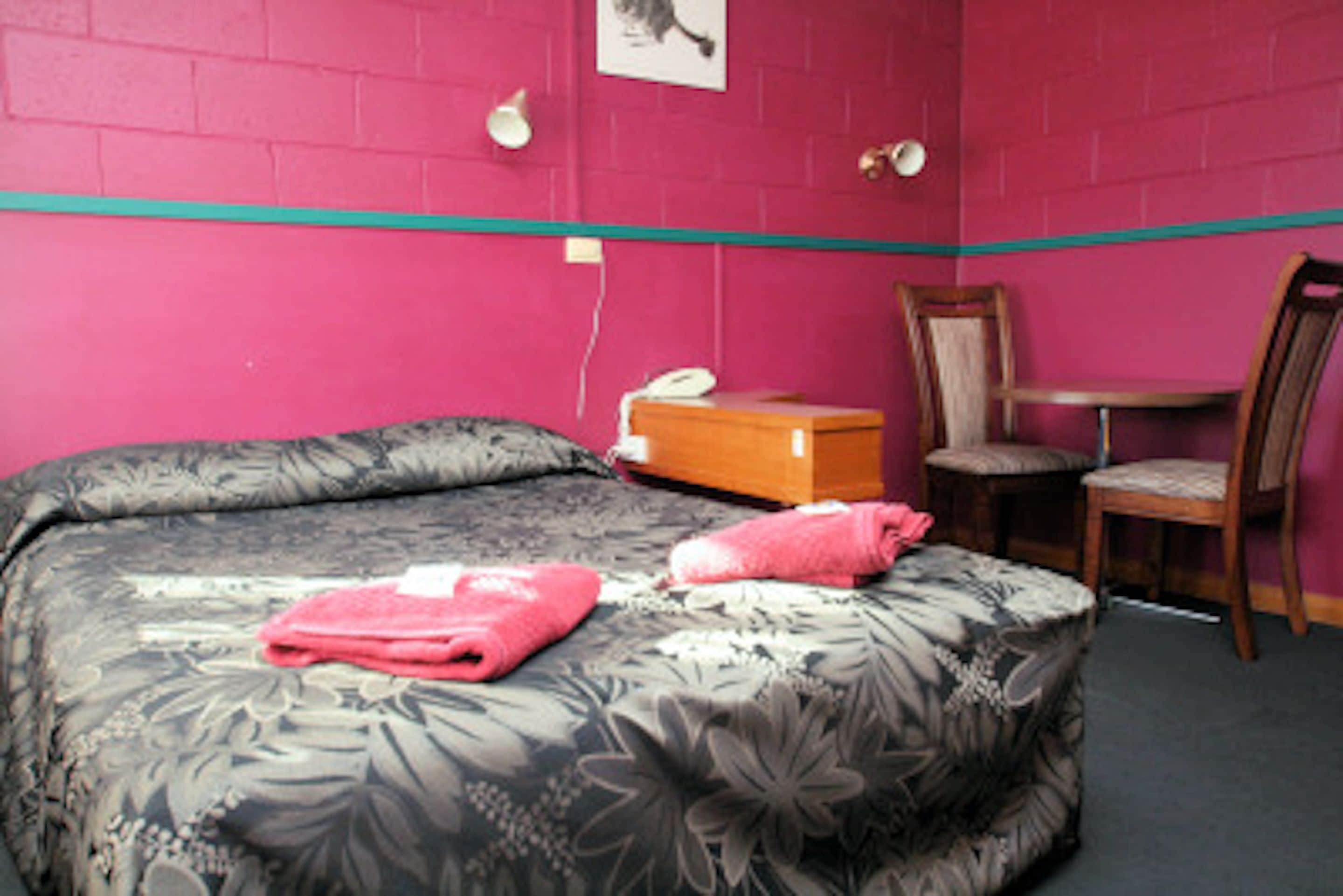 Quarto com cama, cómoda de madeira, cadeira e mesa pequena.