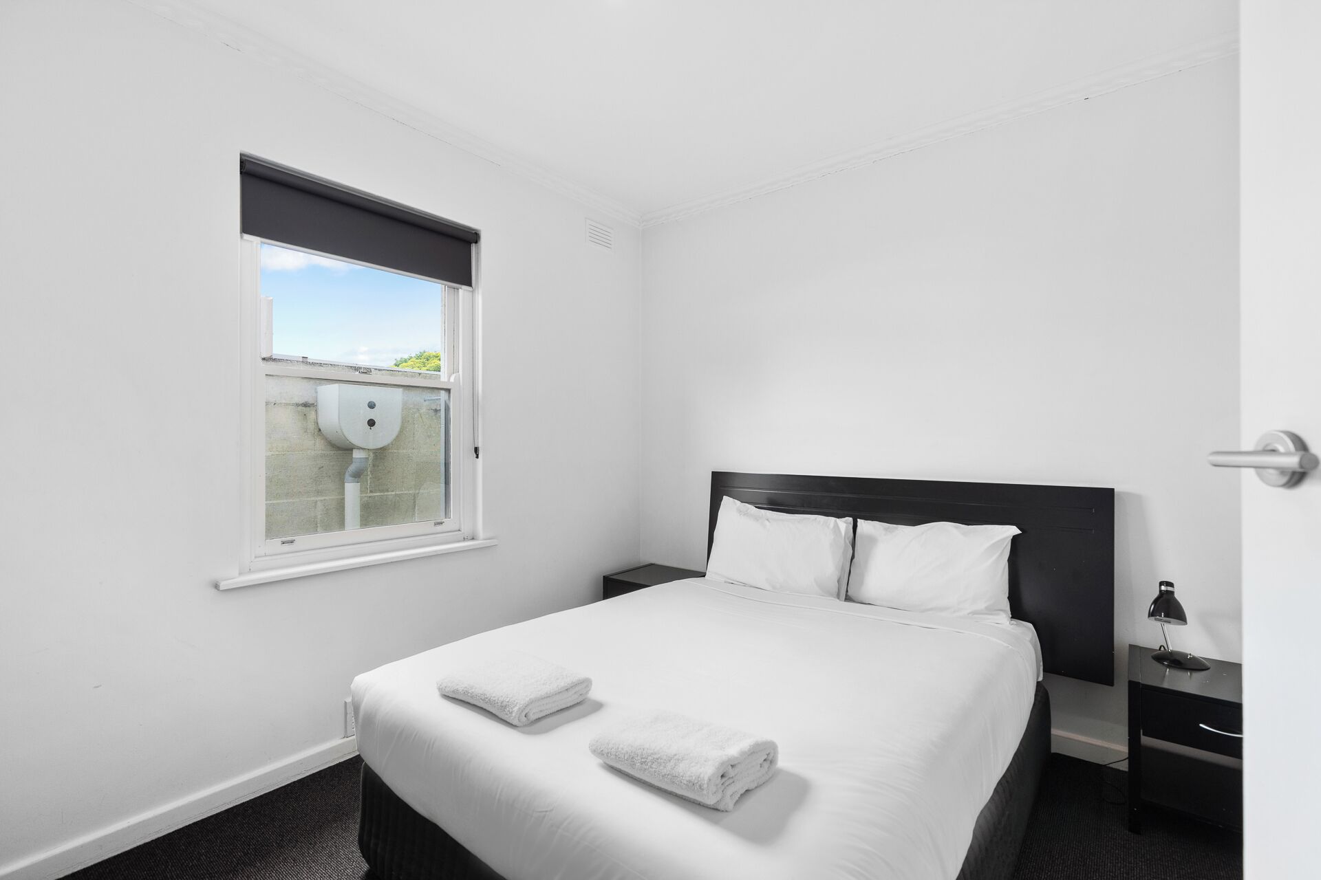 Quarto de hotel com cama, janela com vista, mesa de cabeceira e abajur.