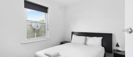Quarto de hotel com cama, janela com vista, mesa de cabeceira e abajur.