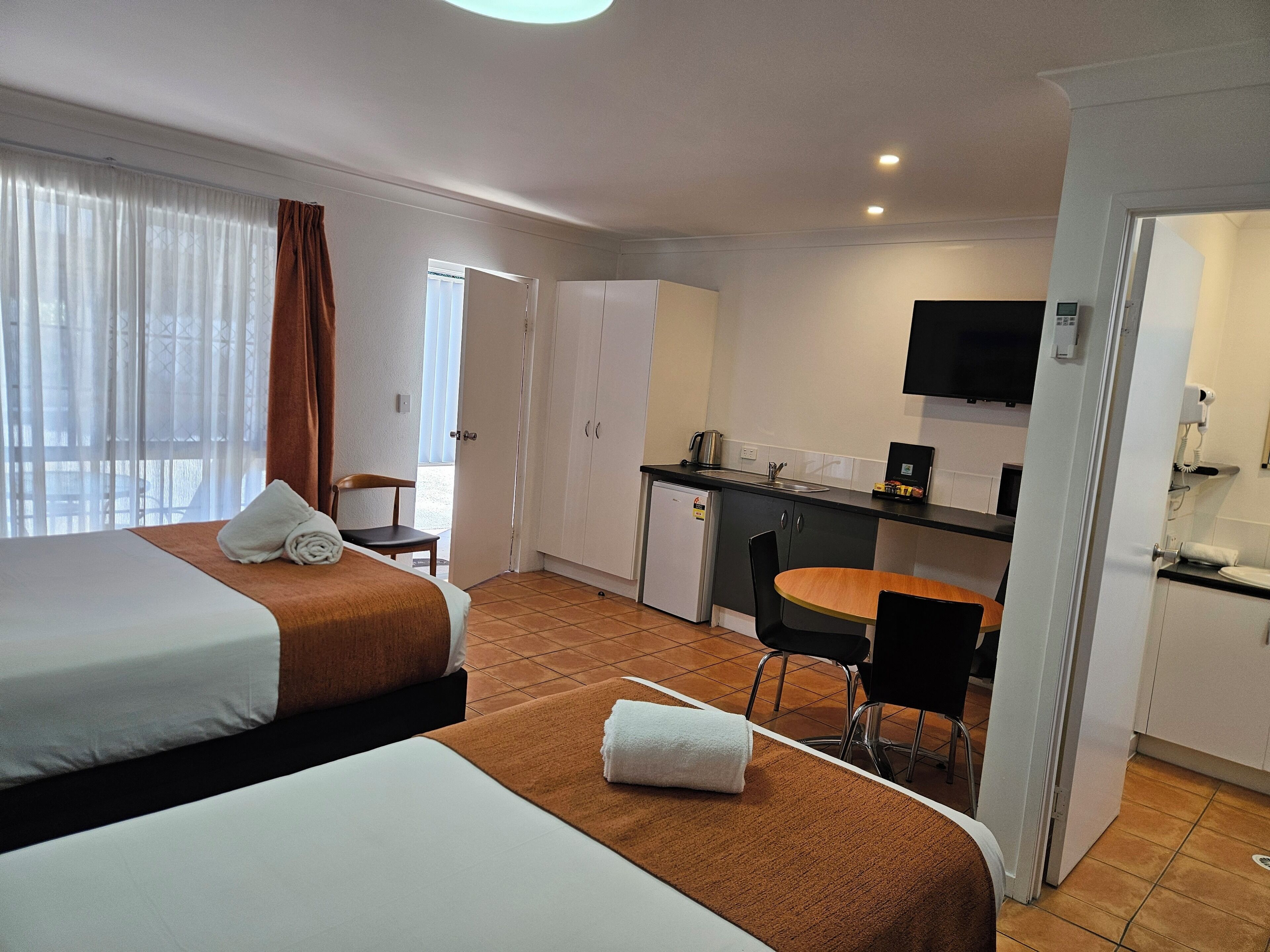 Quarto de hotel com duas camas, uma kitchenette pequena, área de refeições e televisão na parede.