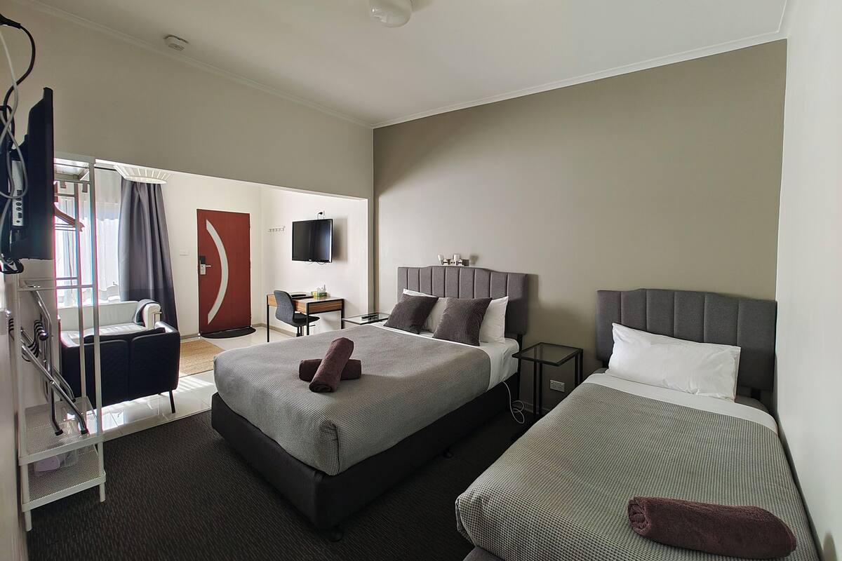Quarto de hotel com duas camas, uma escrivaninha, televisão e zona de chuveiro.