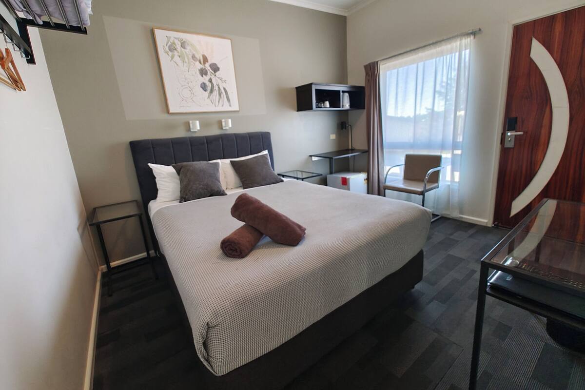 Quarto de hotel com uma cama grande, uma escrivaninha, uma cadeira e uma televisão.