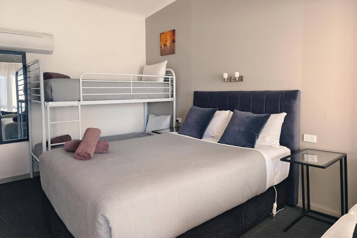 Um quarto com uma cama de solteiro, uma cama individual, uma mesinha de cabeceira e um ar condicionado fixado na parede.