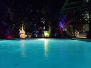 Uma piscina com uma estátua e plantas tropicais.