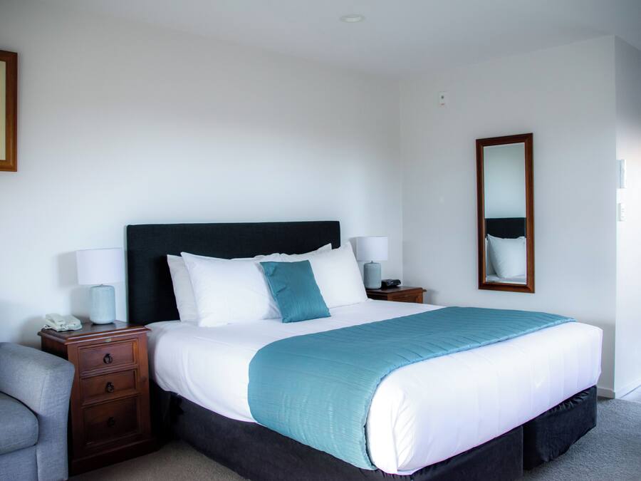 Quarto bem organizado com cama, mesas de cabeceira, cadeira e espelho.