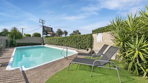 Uma piscina com espreguiçadeiras, cercada por vegetação e um sebedeiro.