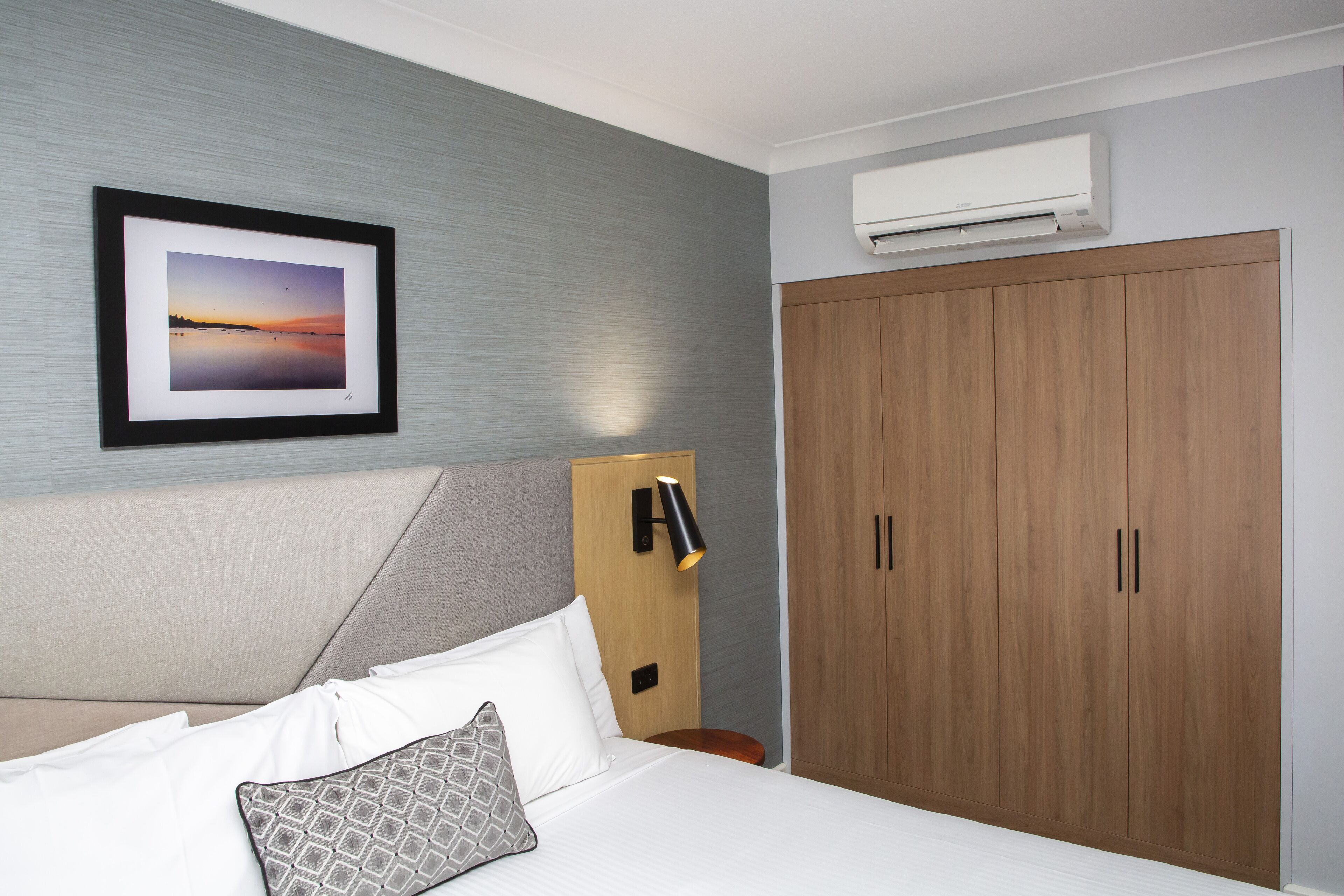 Quarto de hotel bem arrumado com uma cama, um quadro na parede, um guarda-roupa de madeira e um ar condicionado.