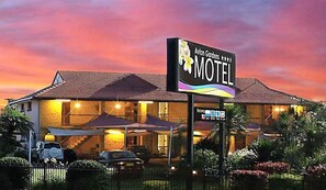 Um motel com uma placa, área de estacionamento coberta e um céu ao pôr do sol.