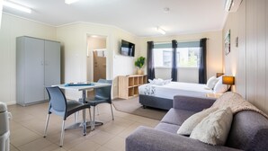 Quarto moderno com cama, escrivaninha, cadeira, sofá e televisão.