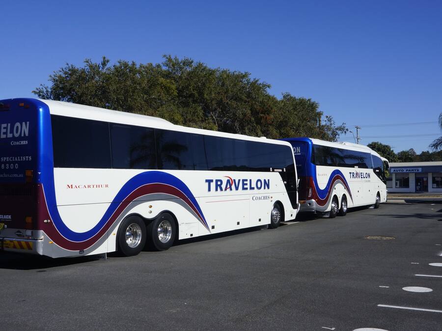 Um ônibus grande branco com detalhes em azul e vermelho estacionado em um estacionamento.