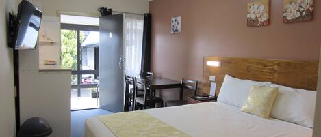 Quarto de hotel com uma cama, escrivaninha, cadeira, televisão e janela com cortinas.