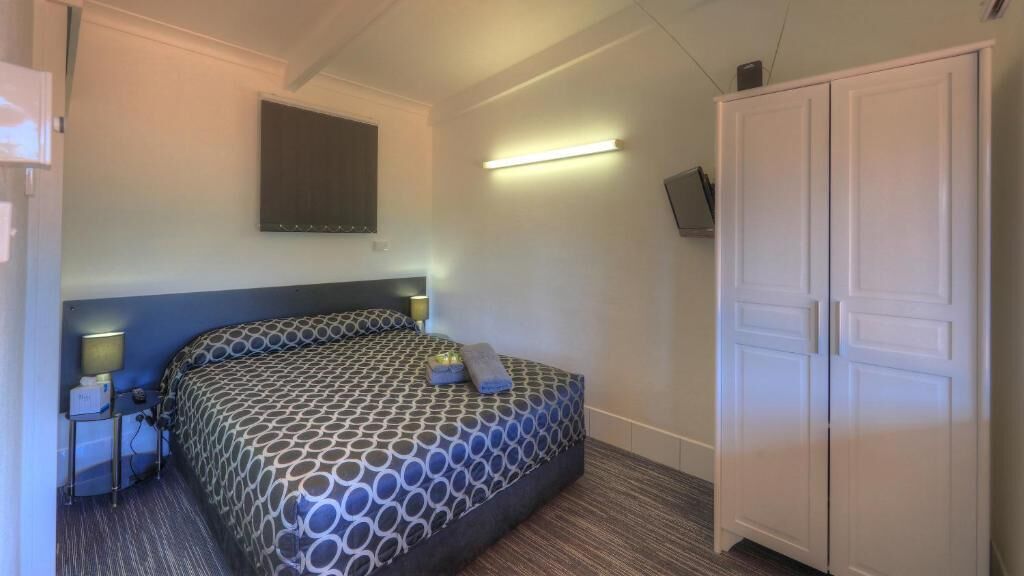 Quarto de hotel com cama, luminárias de cabeceira, guarda-roupa e televisão de tela plana na parede.