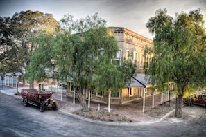 Carro antigo estacionado em frente a um edifício de arquitetura clássica, rodeado por árvores.