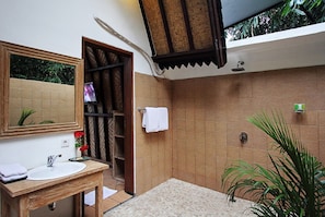 Uma casa de banho com toucador de madeira, um espelho grande, chuveiro e chão em azulejo.