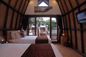 Quarto com duas camas, teto de madeira e vista para uma casa através de uma grande janela.