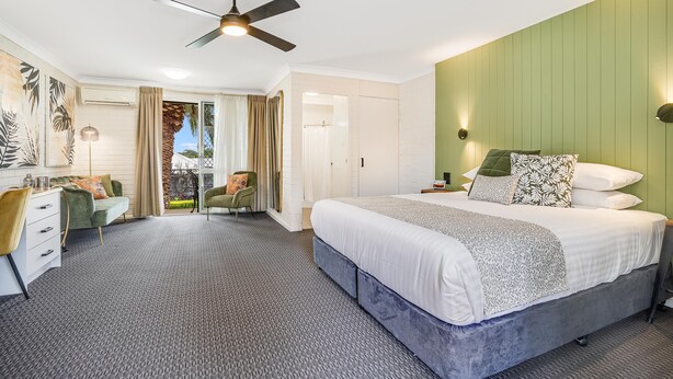 Quarto espaçoso com cama grande, ventilador de teto, escrivaninha com cadeira e vista para o exterior.