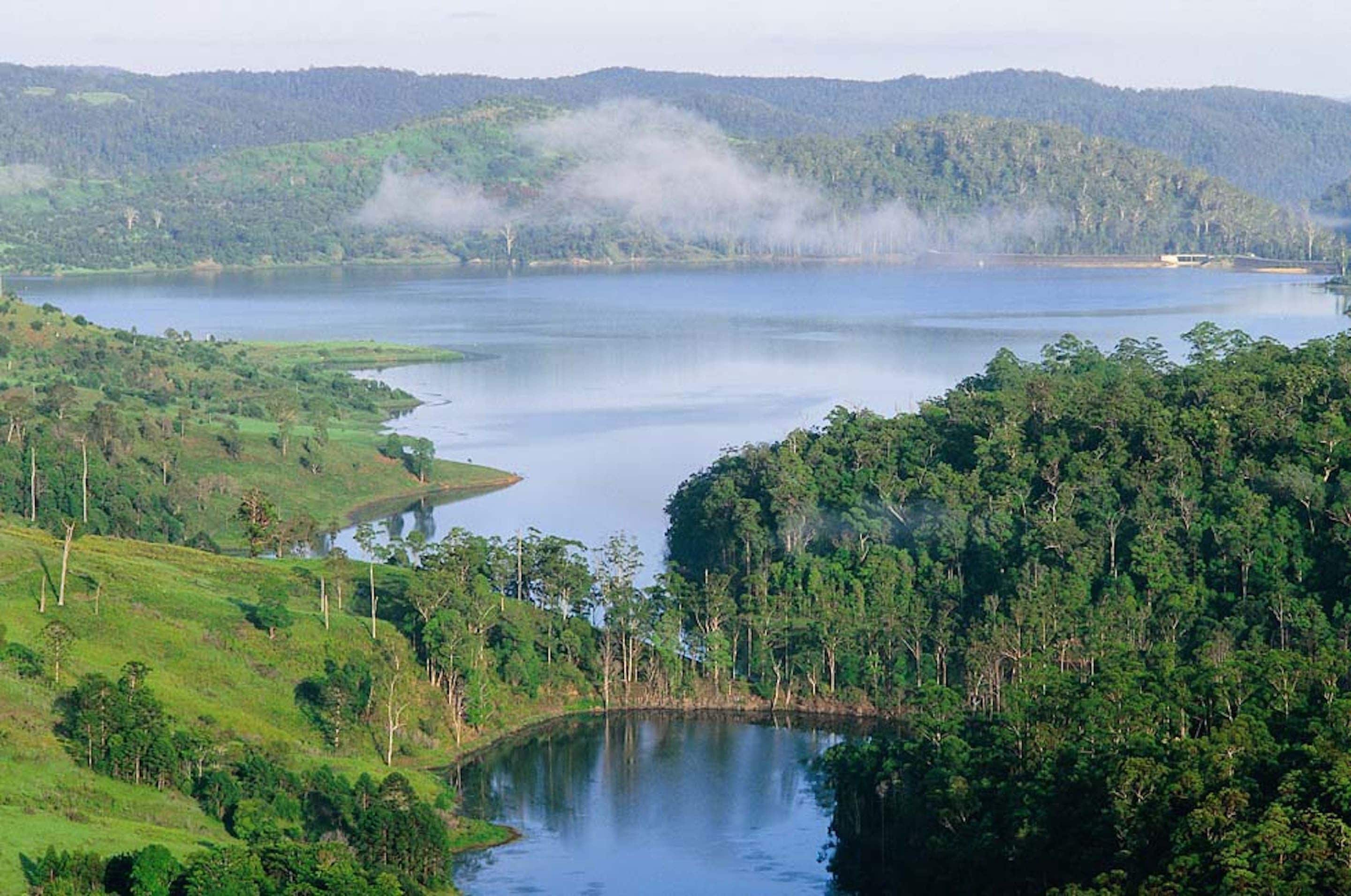 Um lago tranquilo rodeado por vegetação exuberante e colinas arborizadas.