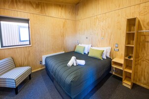 Quarto com cama, um banquinho e guarda-roupa de madeira.