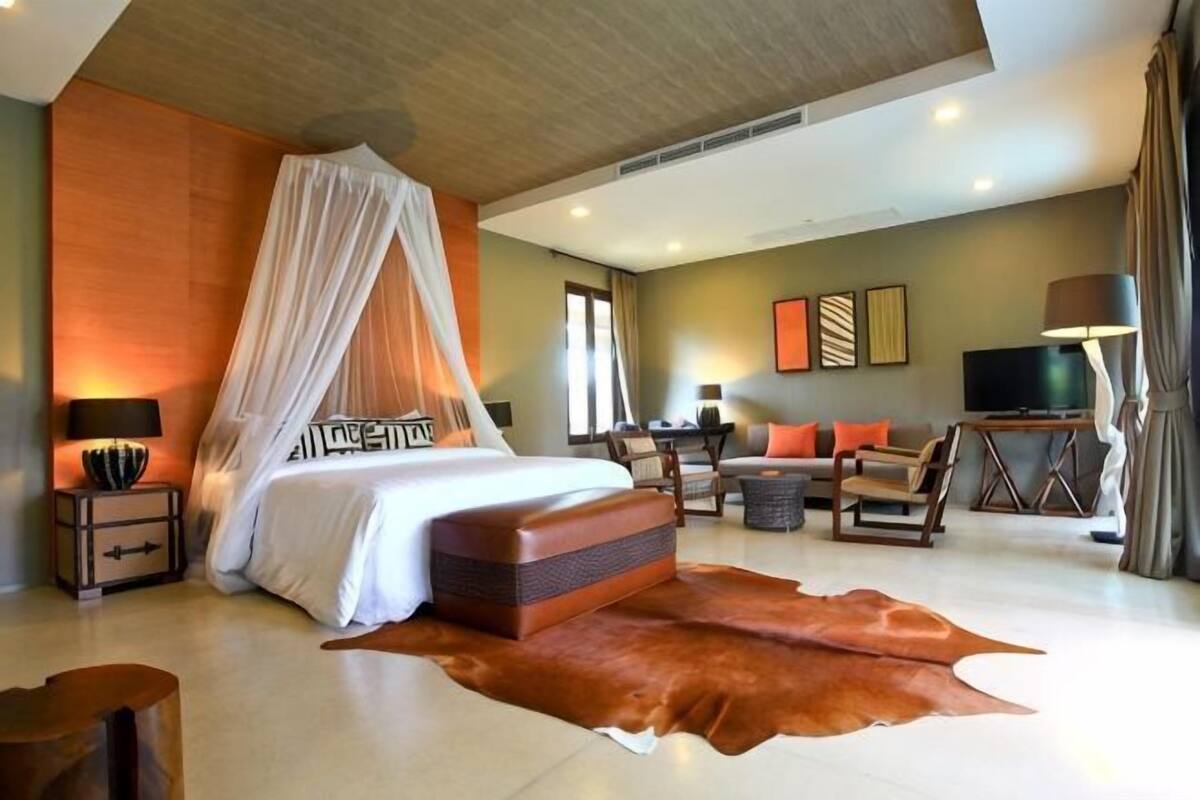 Quarto com cama de dossel, sofá de couro, TV e escrivaninha.