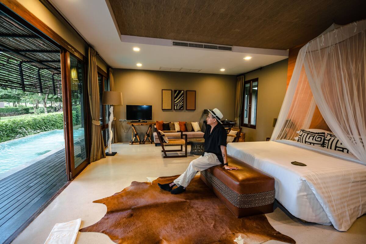 Quarto moderno com cama grande, sofá, televisão e vista para uma piscina.