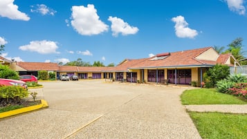 Um motel com acesso por um caminho de cascalho, vários quartos com telhados de telha vermelha e um estacionamento.