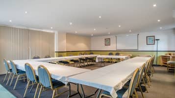 Uma sala de conferência com mesas e cadeiras compridas, uma tela de projeção e um projetor de slides.