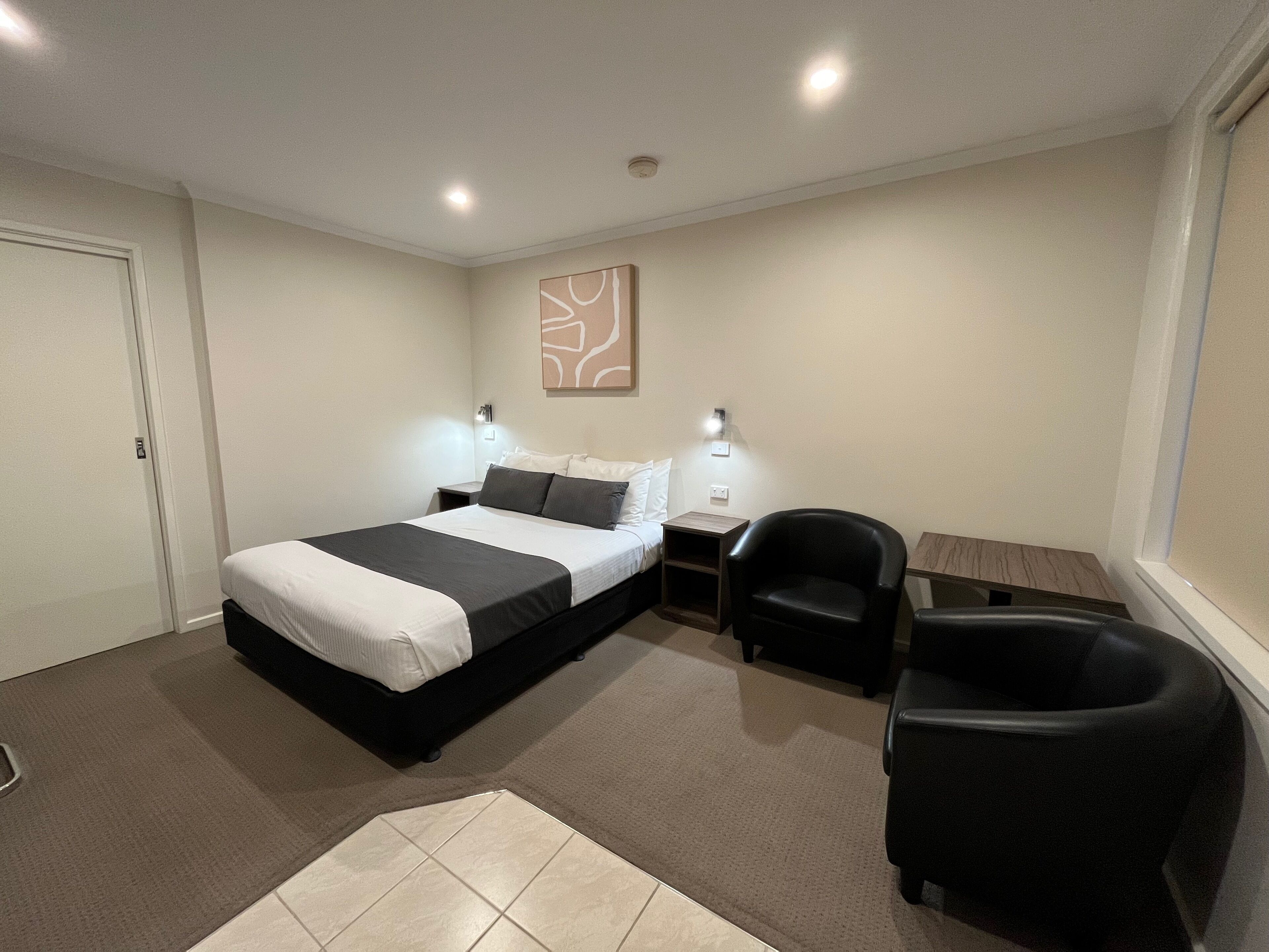 Quarto de hotel moderno com uma cama grande, uma escrivaninha, uma cadeira e uma mesinha.
