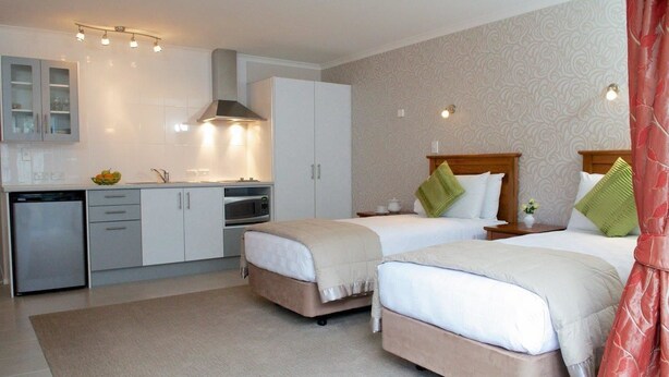Quarto de hotel com duas camas, uma cozinha compacta e banheiro.
