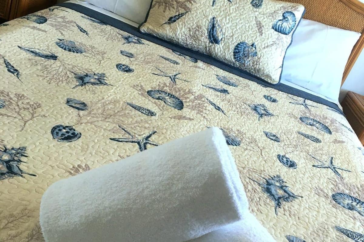 Uma cama com colcha temática do mar, travesseiros e uma toalha branca enrolada.