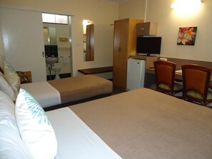 Quarto de hotel com duas camas, uma escrivaninha com computador, televisão e um pequeno frigorífico.