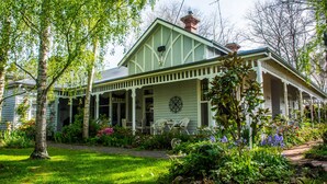 Uma casa de dois andares com varanda, rodeada por vegetação exuberante e plantas floridas.