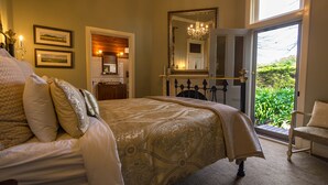 Quarto com uma cama grande, um candelabro, um espelho e vista para o verde através de uma porta.