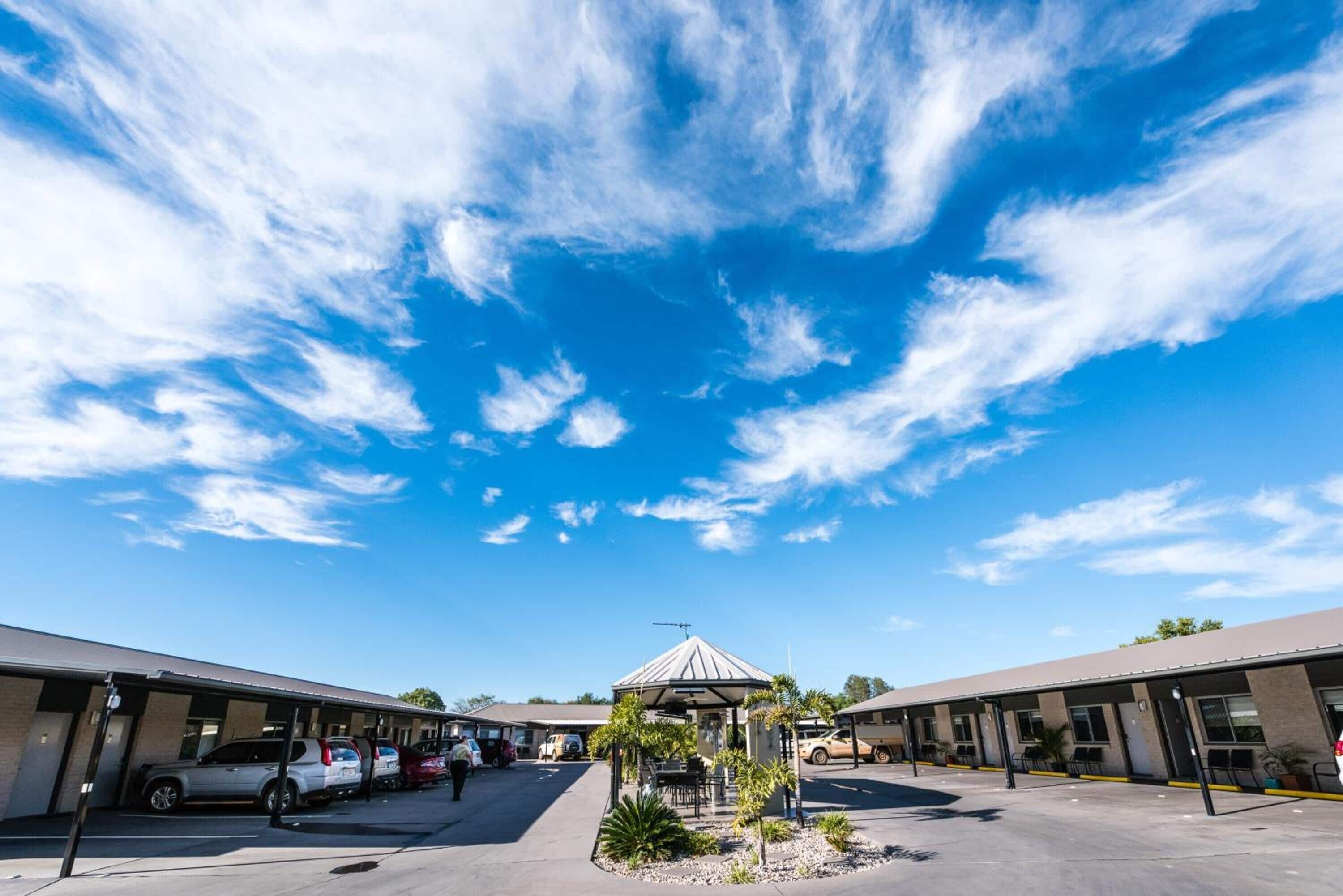 Um motel com área de estar coberta ao ar livre, estacionamento e céu azul com nuvens.