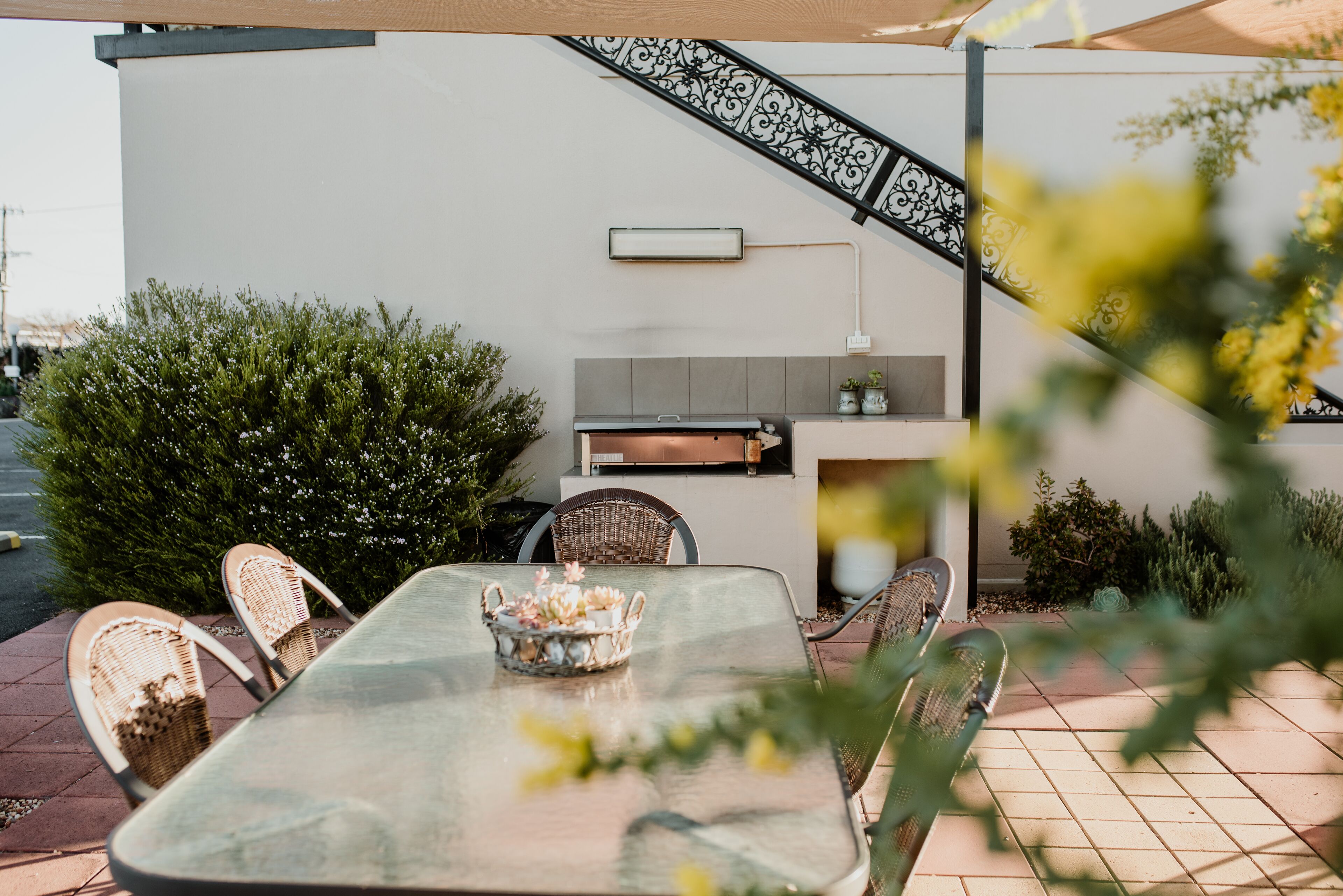 Um pátio ao ar livre com mesa e cadeiras, churrasqueira embutida e escada com guarda-corpos decorativos.