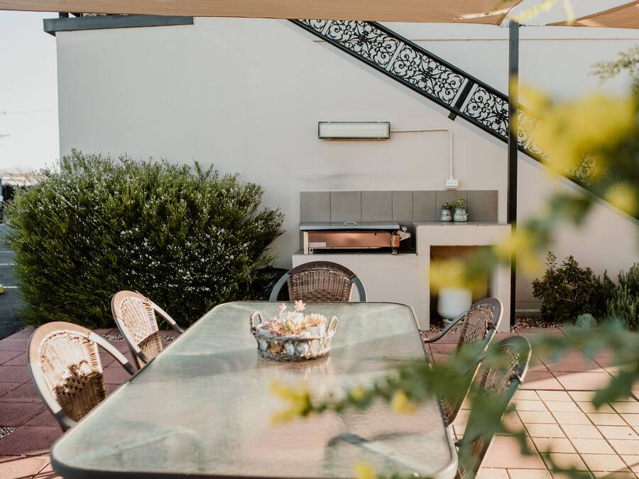Um pátio ao ar livre com mesa e cadeiras, churrasqueira embutida e escada com guarda-corpos decorativos.