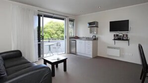Apartamento moderno com sala de estar, cozinha compacta e varanda com vista para o verde.
