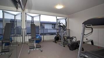 Academia com equipamentos de ginástica, esteira e uma grande janela com vista para a cidade.