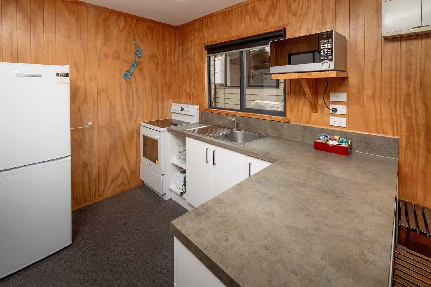Cozinha compacta com paredes de madeira, forno embutido, micro-ondas e pia.