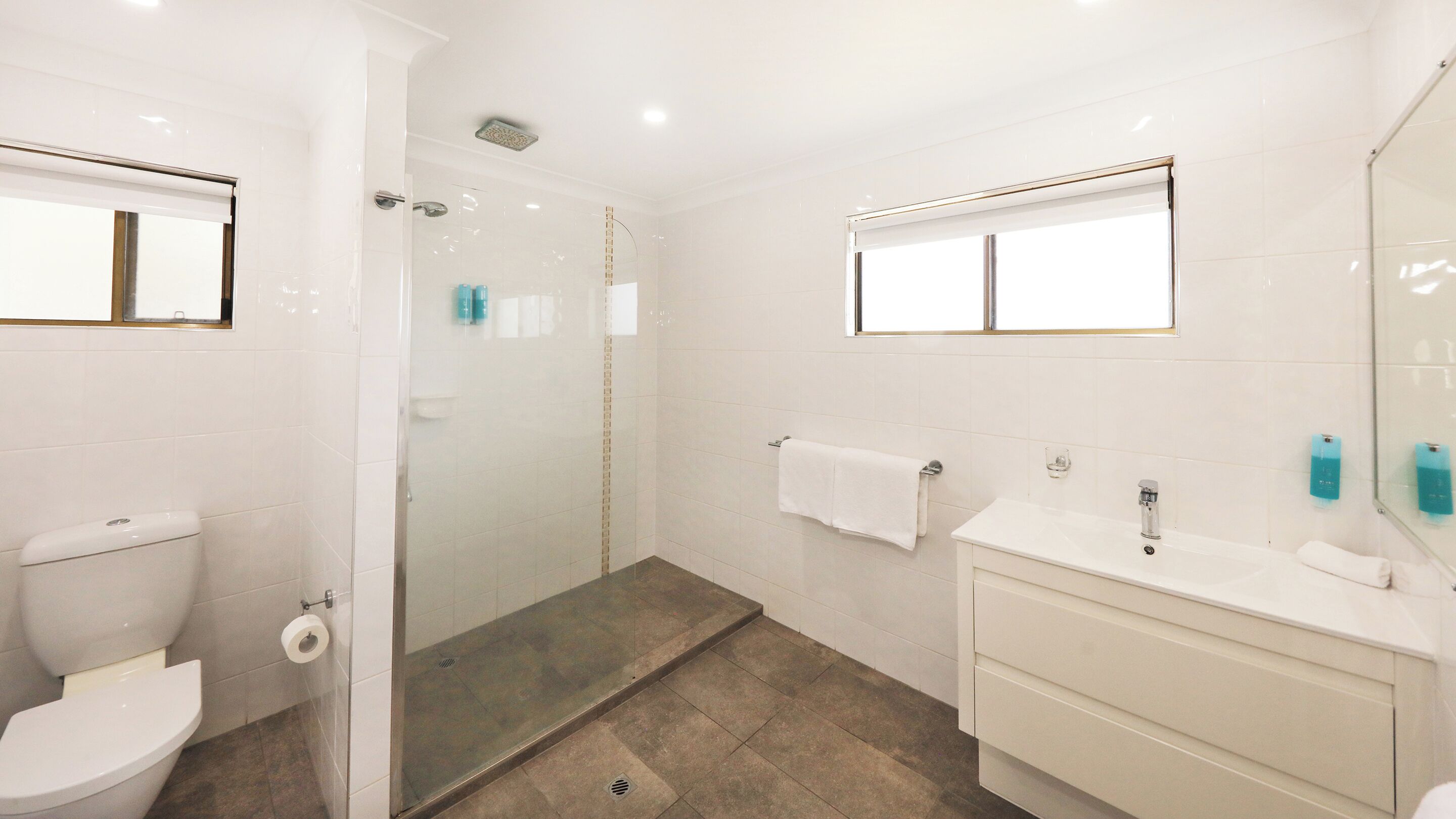 Casa de banho moderna com chuveiro envidraçado, sanita, lavatório com espelho e toucador com gavetas.