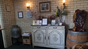 Quarto nos fundos com parede de tijolos, um relógio, quadros emoldurados, um armário com objetos decorativos, um barril de madeira e uma cadeira de vime.